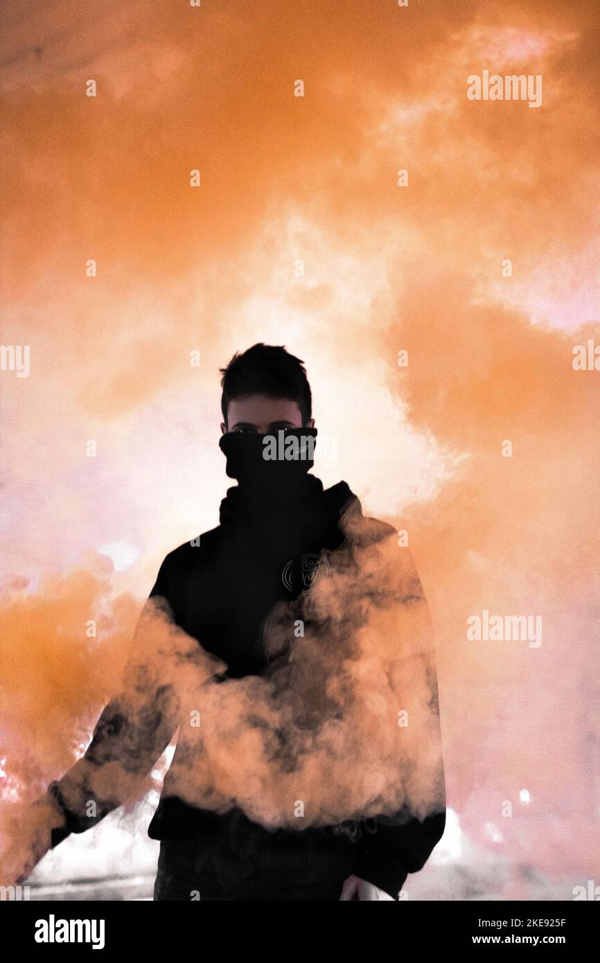 A vertical shot of a young boy with a mask carrying an orange smoke ...