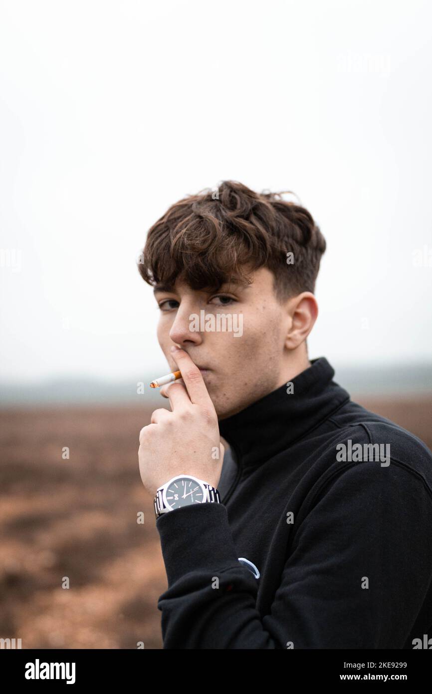 A vertical shot of a young Caucasian boy smoking a cigarette standing ...