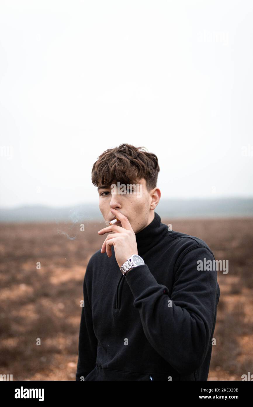 A vertical shot of a young Caucasian boy smoking a cigarette standing ...