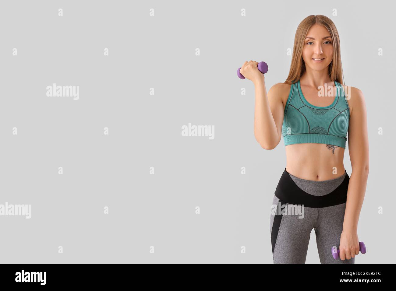 Sporty young woman with dumbbells on light background Stock Photo - Alamy