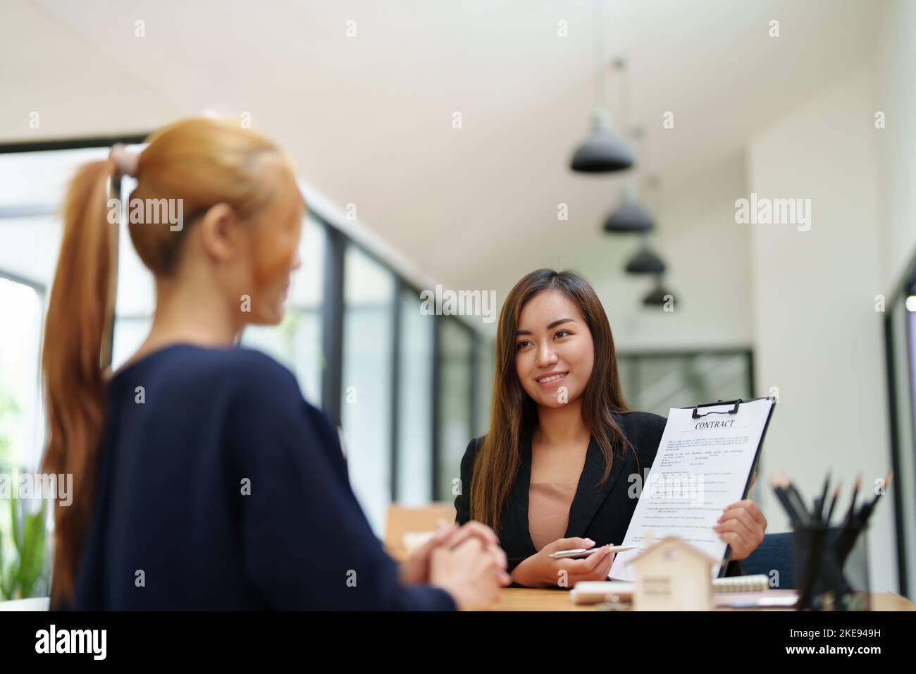 Portrait of an Asian female bank employee asking a customer to read the ... Portrait of an Asian female bank employee asking a customer to read the ...