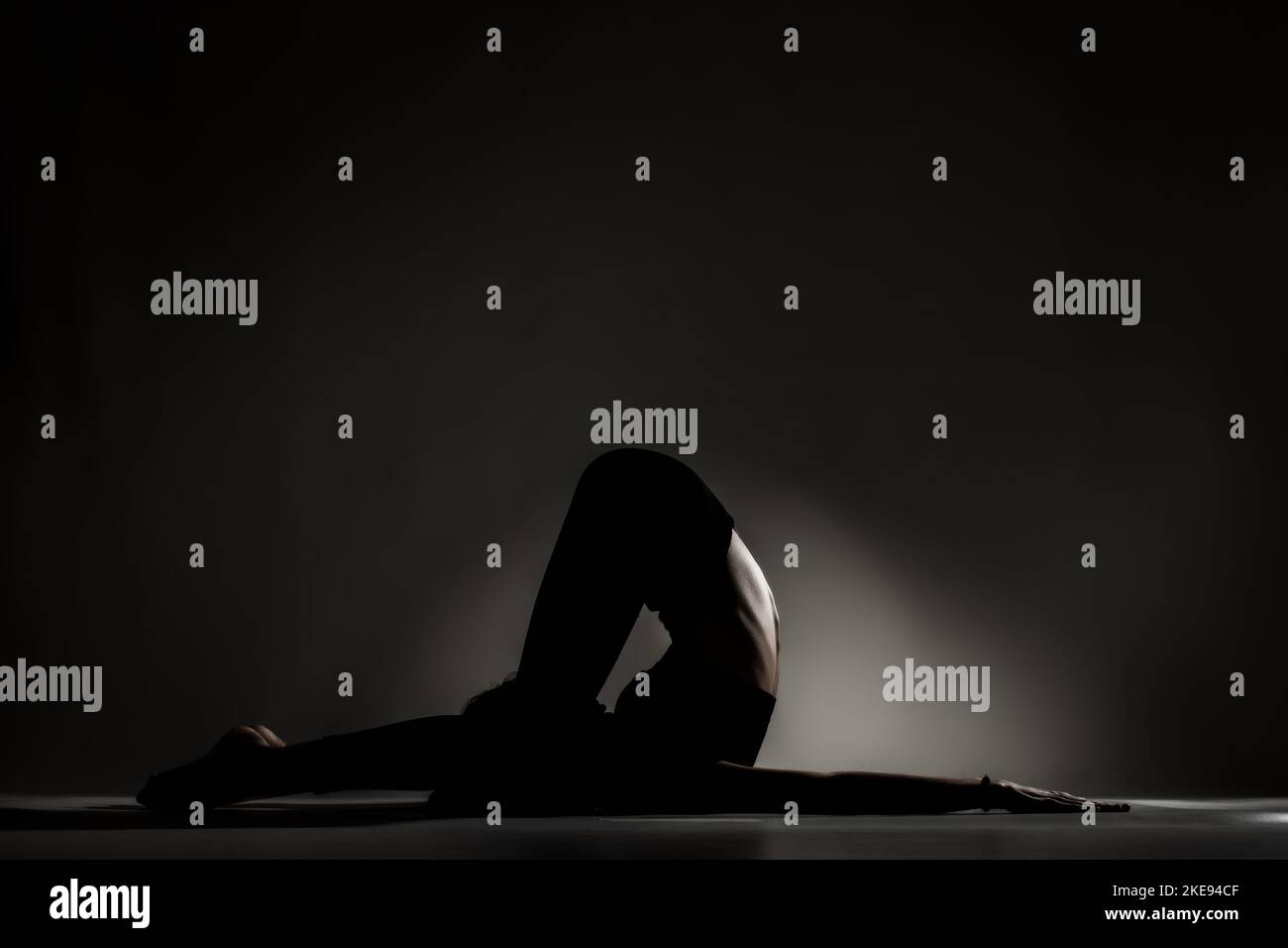 Fit ballerina girl lying and stretching practicing yoga poses. Side lit ...