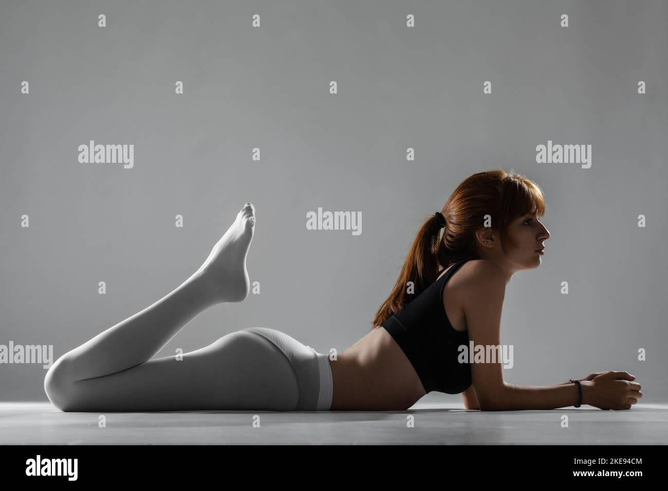 Fit ballerina girl lying and stretching practicing yoga poses against gray background Stock ...