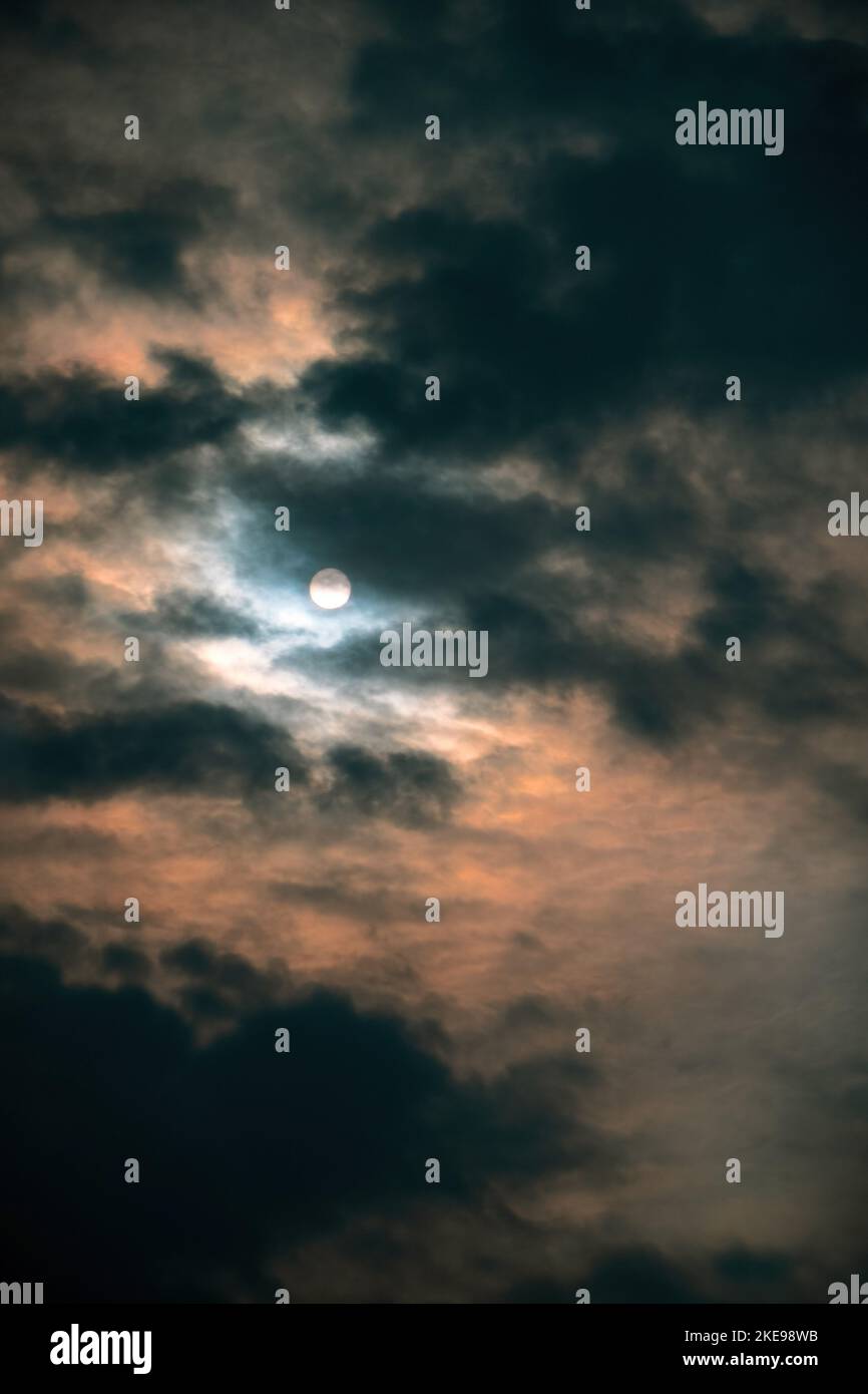 A vertical shot of the Moon against a dramatic cloudy sky at night ...