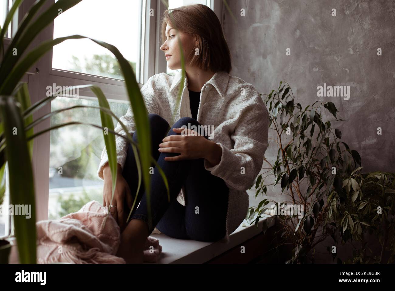 Calm, thoughtful romantic young woman looking out window, sit on ...