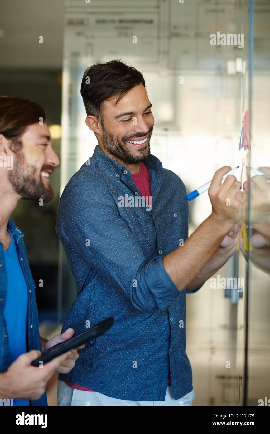 Mapping out their design. two young businessmen brainstorming on a glass wall while standing in ...