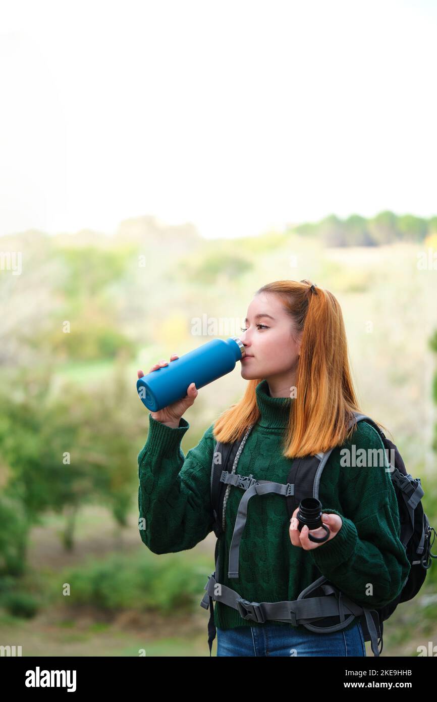 Hiker redhead woman drinking water from canteen wearing a backpack ...