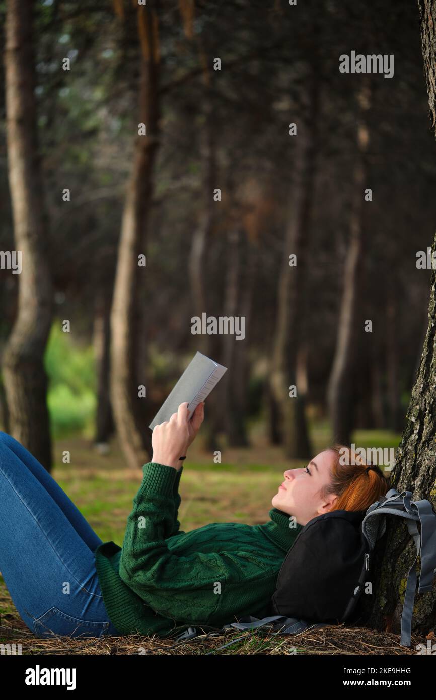 Redhead young woman reading a book lying under tree in forest Stock ...