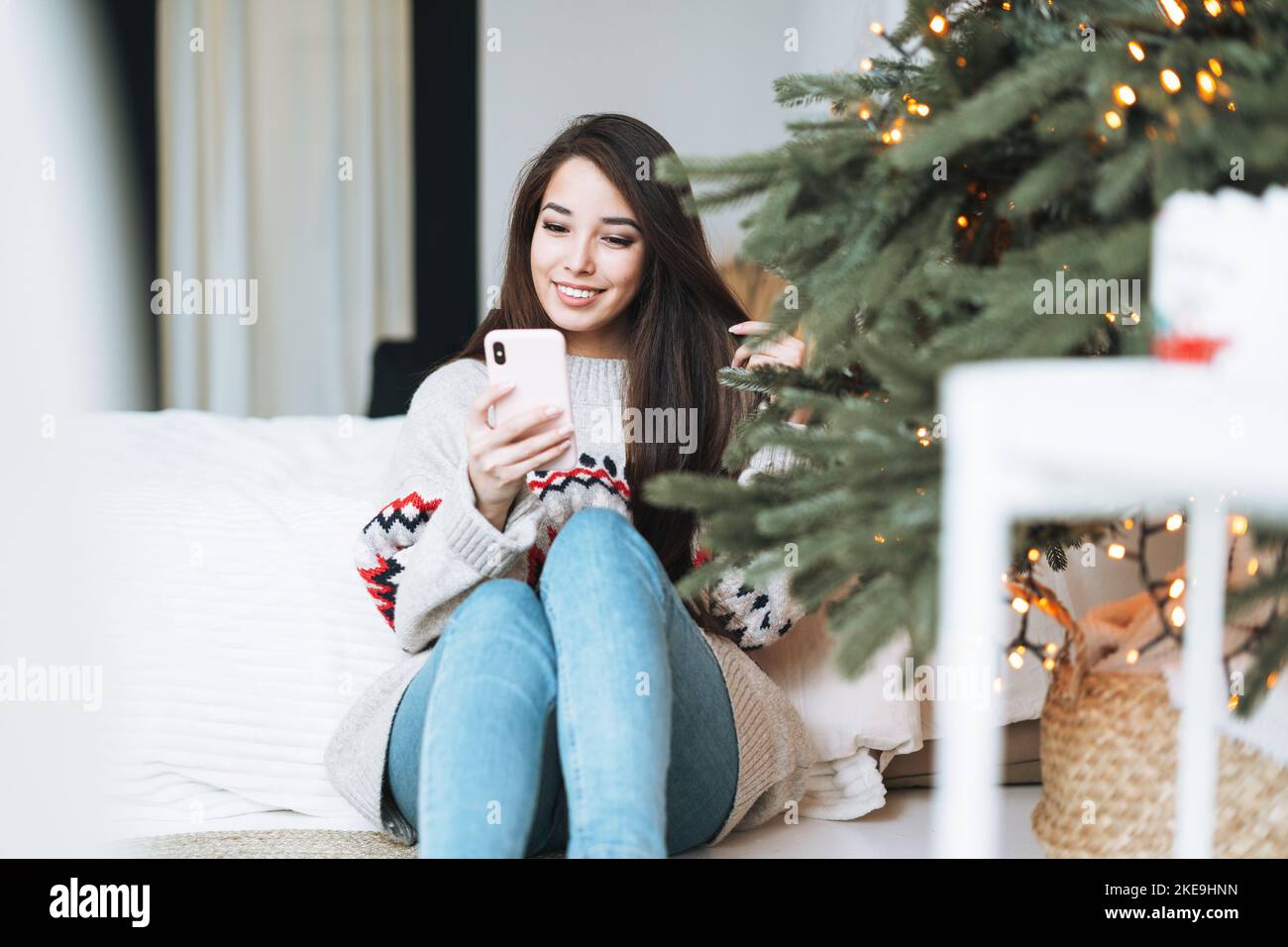 Young beautiful asian woman with dark long hair in cozy sweater using ...
