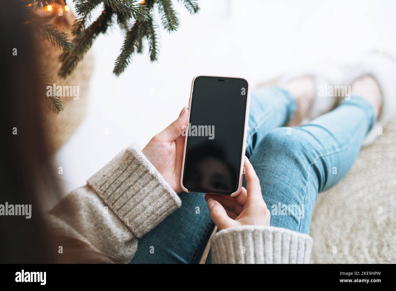 Young woman in cozy sweater using mobile smartphone in room with ...