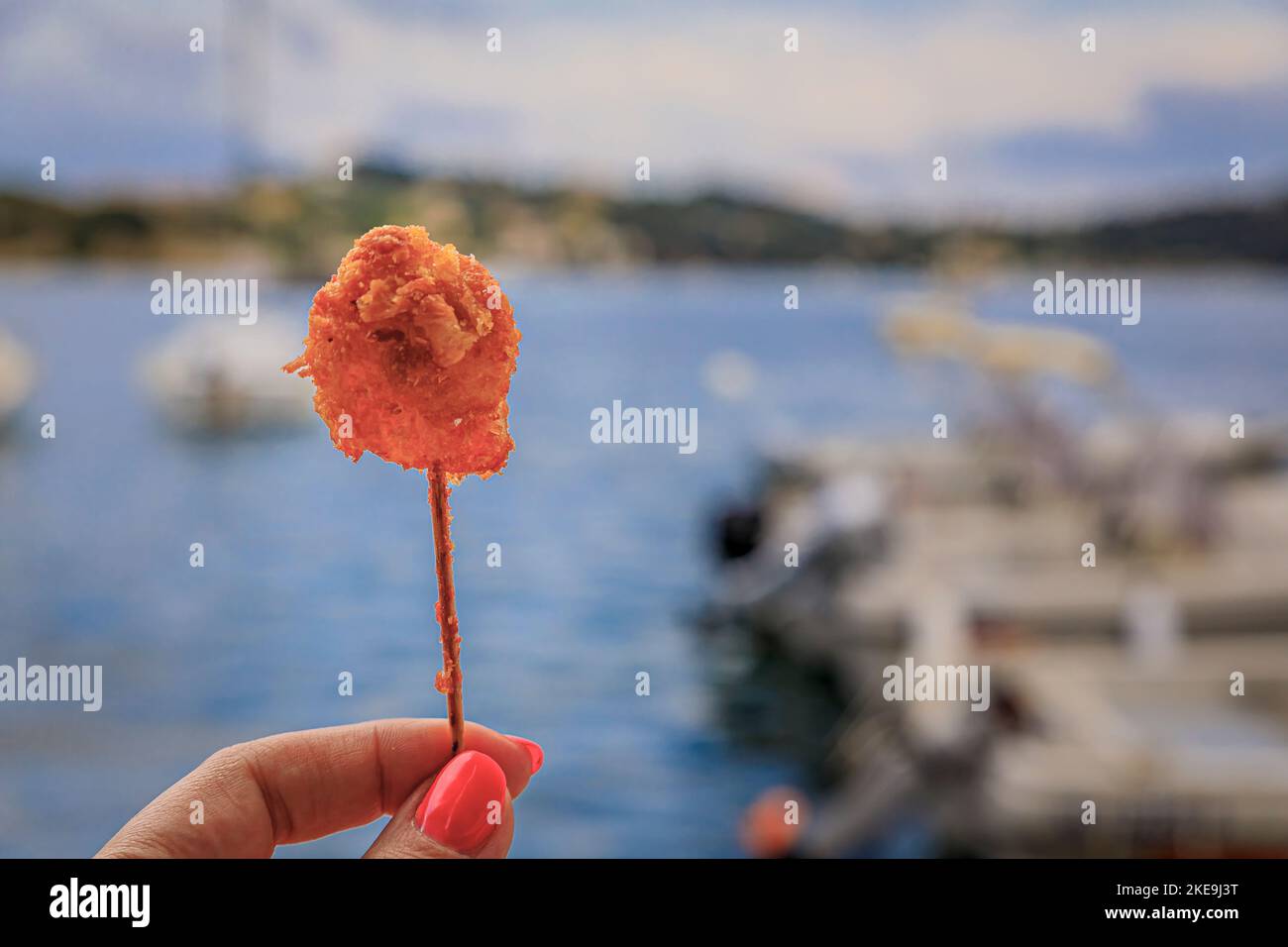 Crispy shrimp fritter on a stick with Mediterranean Sea and boats in ...