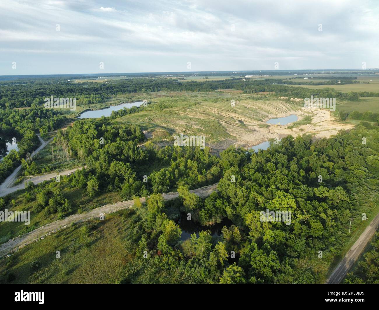 An aerial view of greenery field surrounded by dense trees and water ...