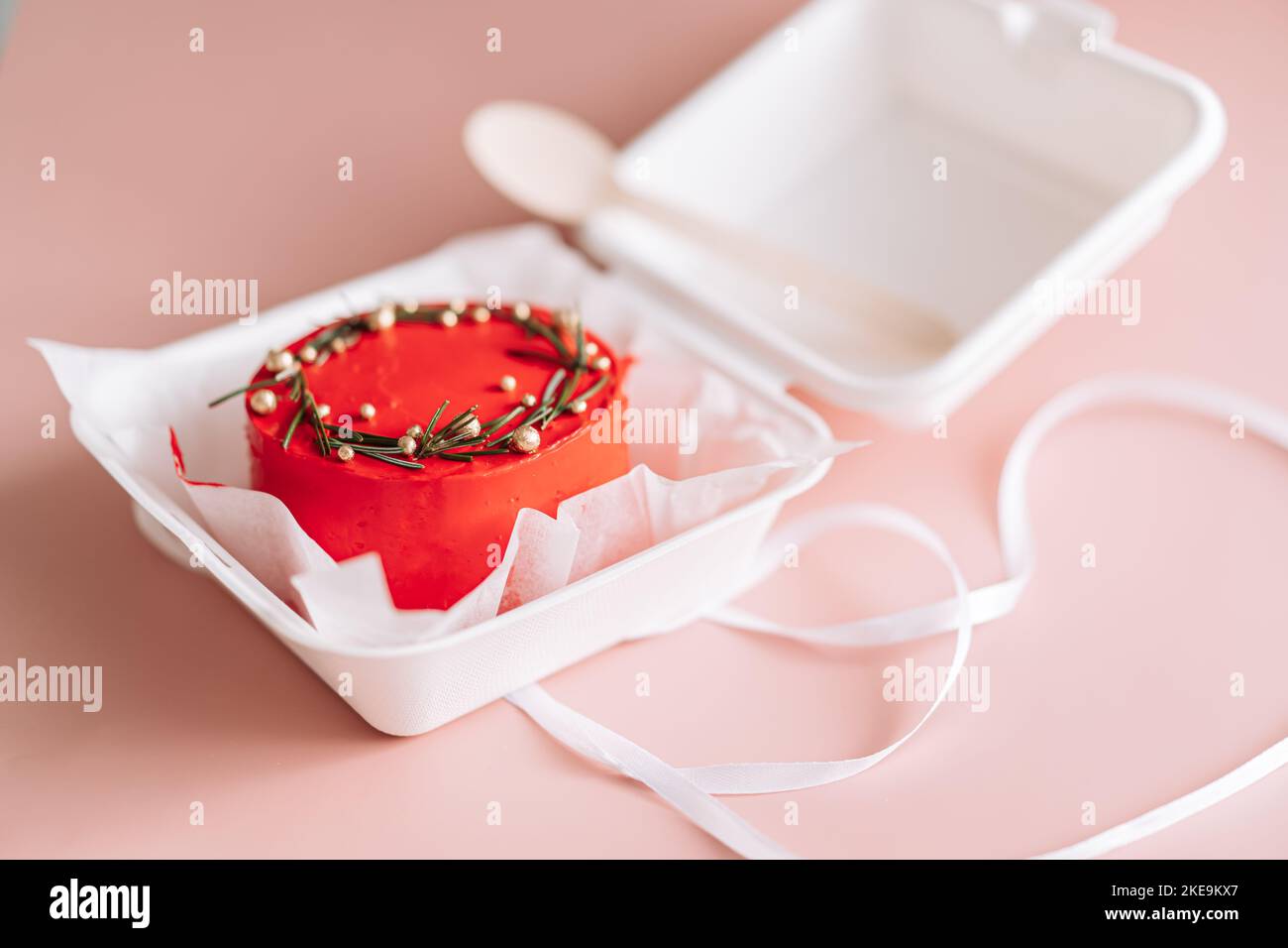Bento cake red color in a white container next to a Christmas tree ...