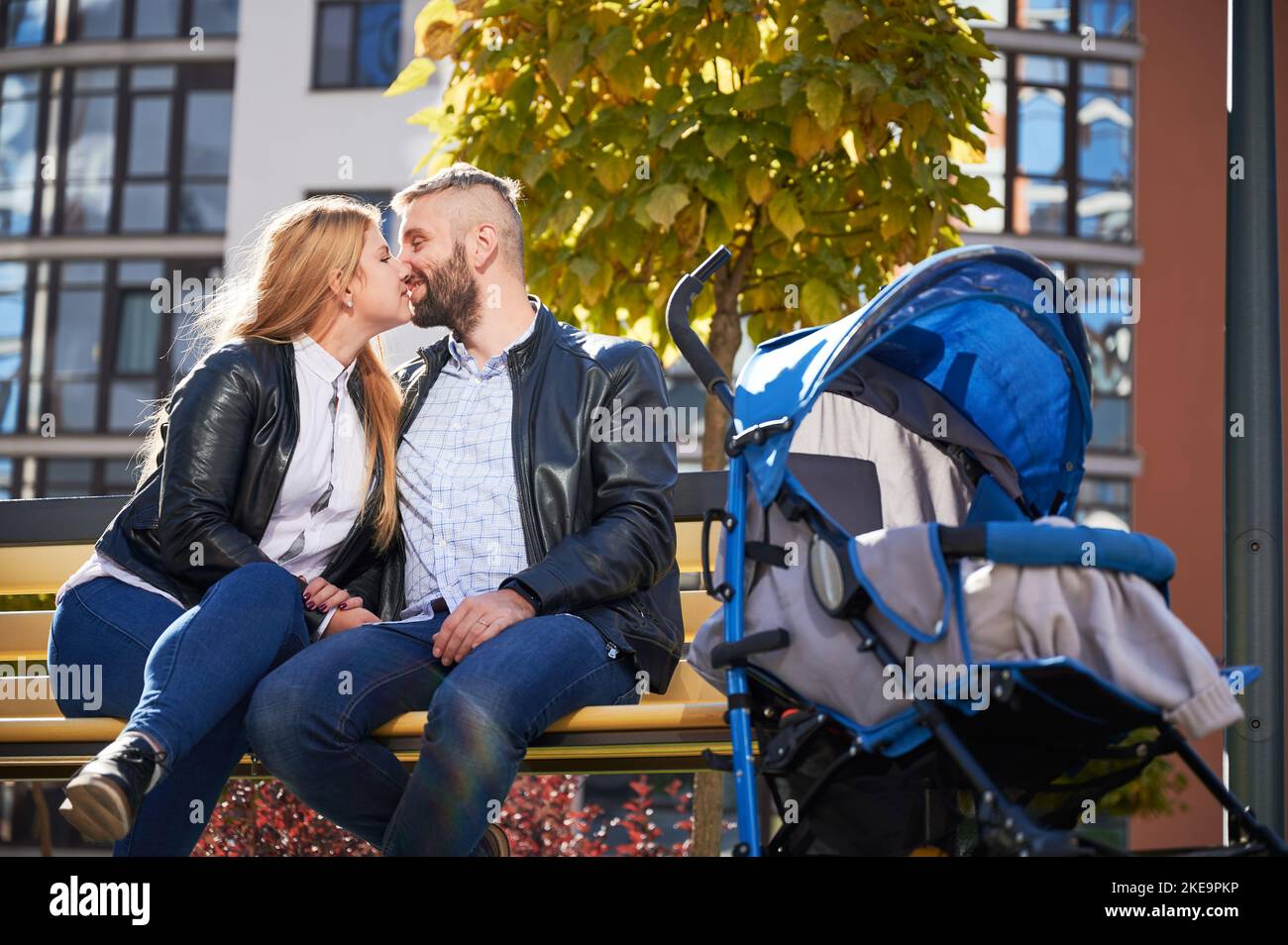 Happy family sitting with unrecognizable baby in blue pram, hugging ...