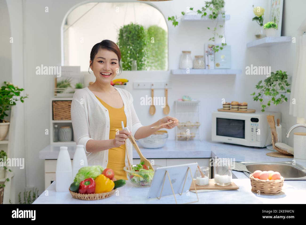 Portrait of smiling young lady cooking fresh organic salad at home in ...