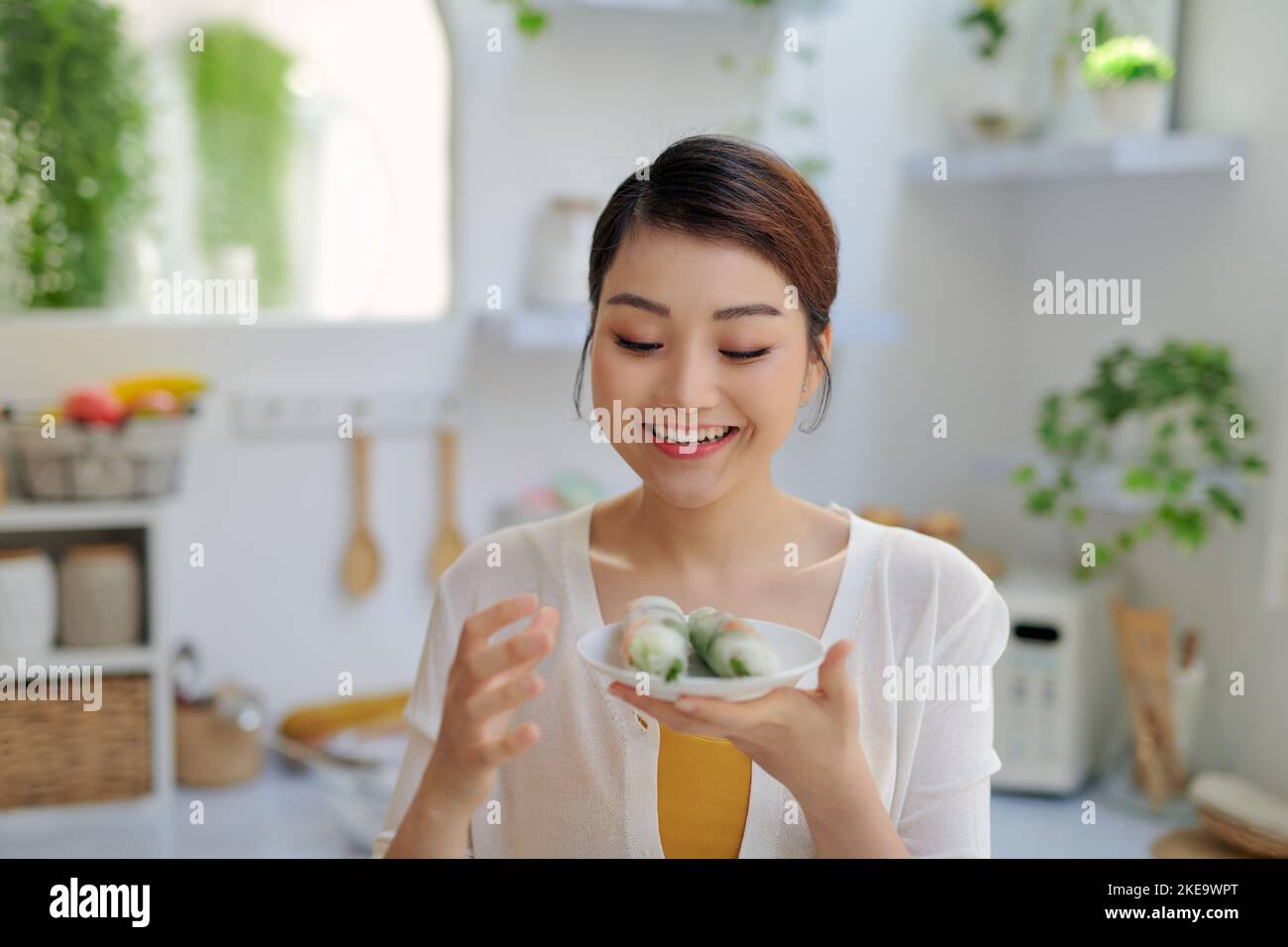 Asian woman eating spring rolls on kitchen background Stock Photo - Alamy