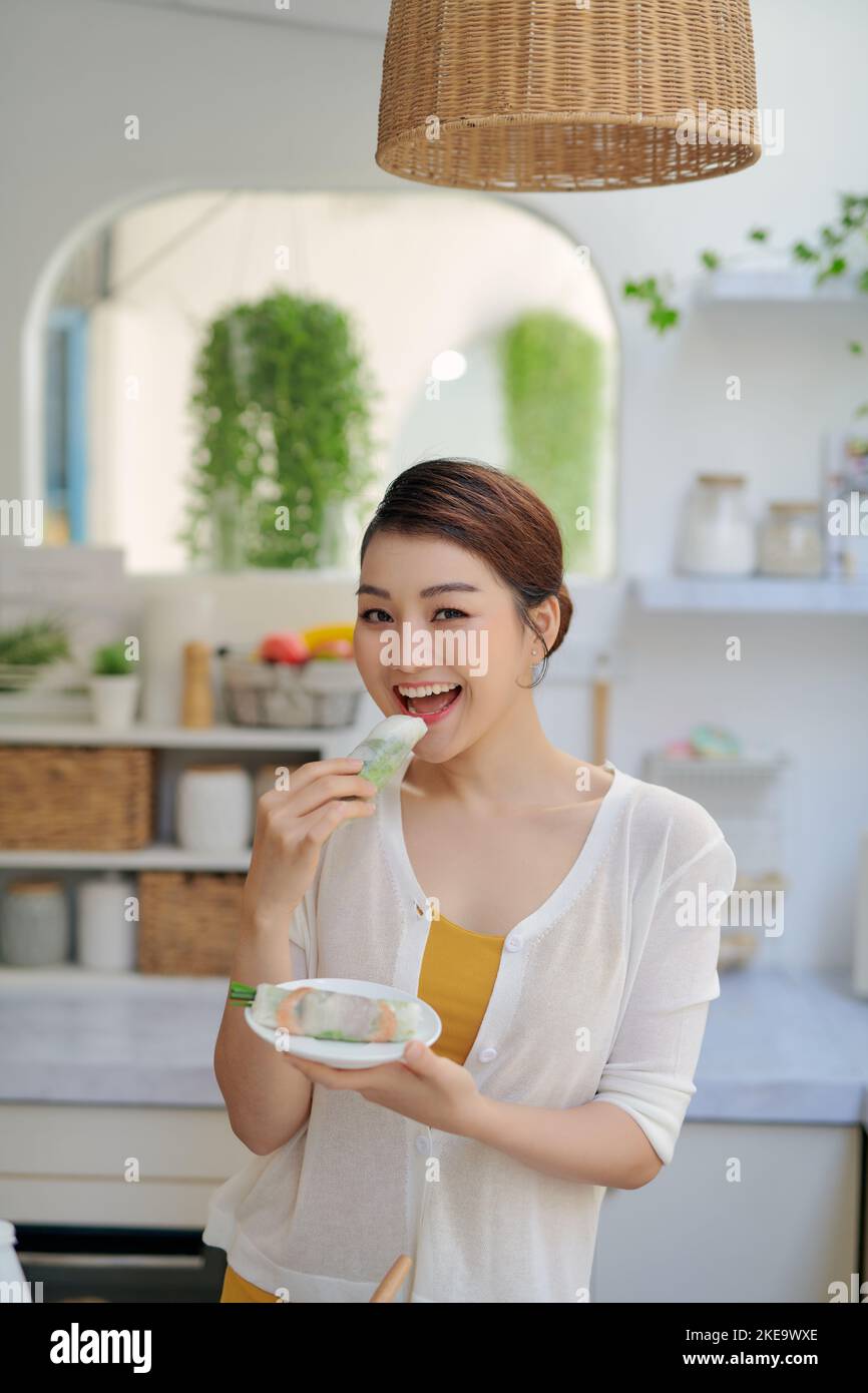 Asian woman eating spring rolls on kitchen background Stock Photo - Alamy