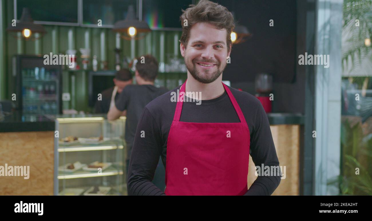 One happy male barista wearing apron standing inside coffee shop ...