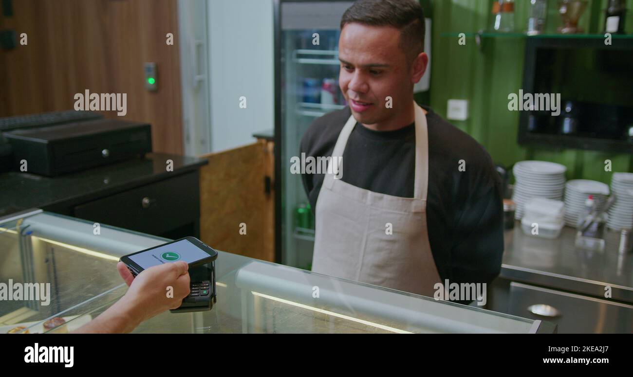 Person paying with cellphone at coffee shop counter. Barista handing ...