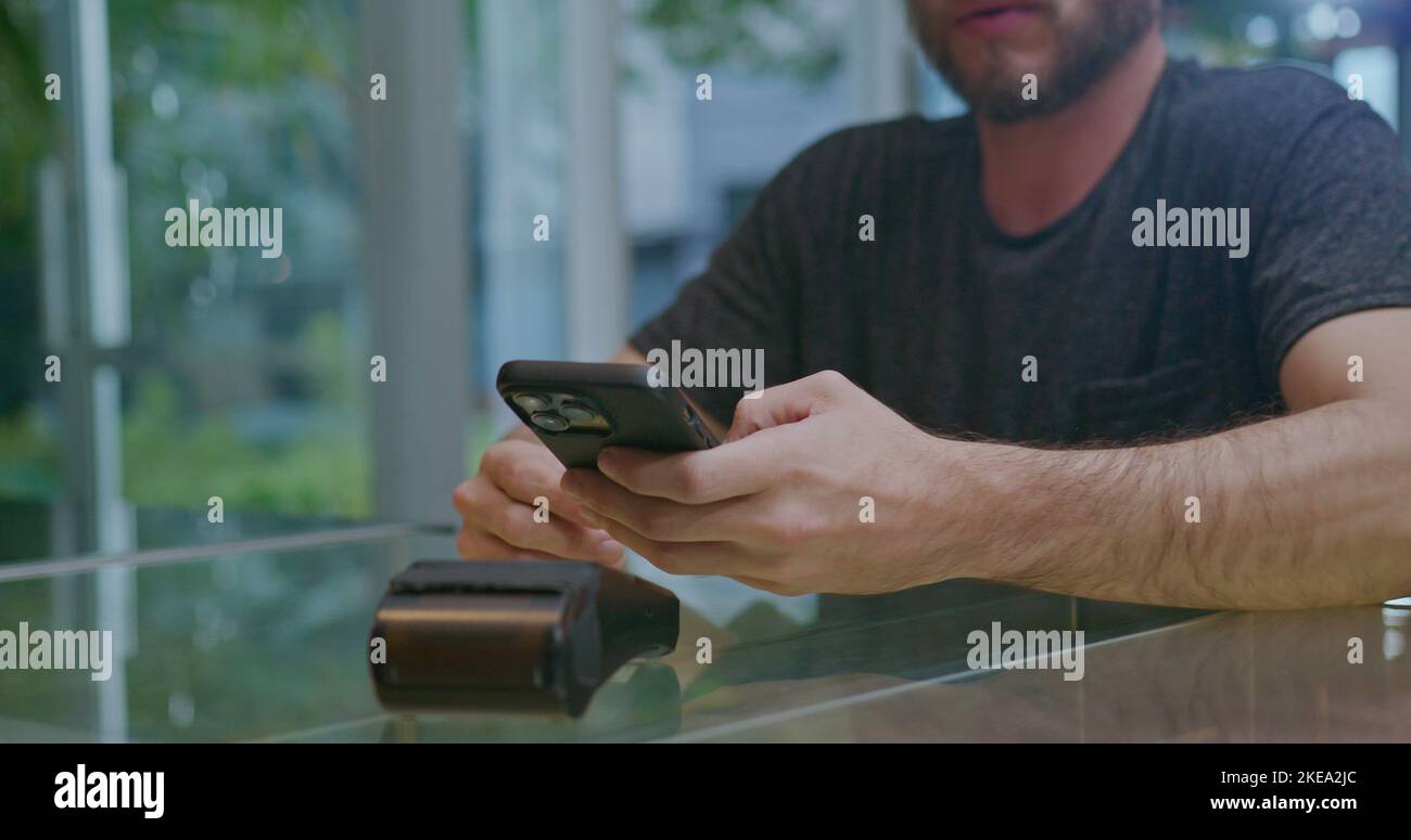 Young man paying with cellphone at coffee shop counter. Barista handing ...