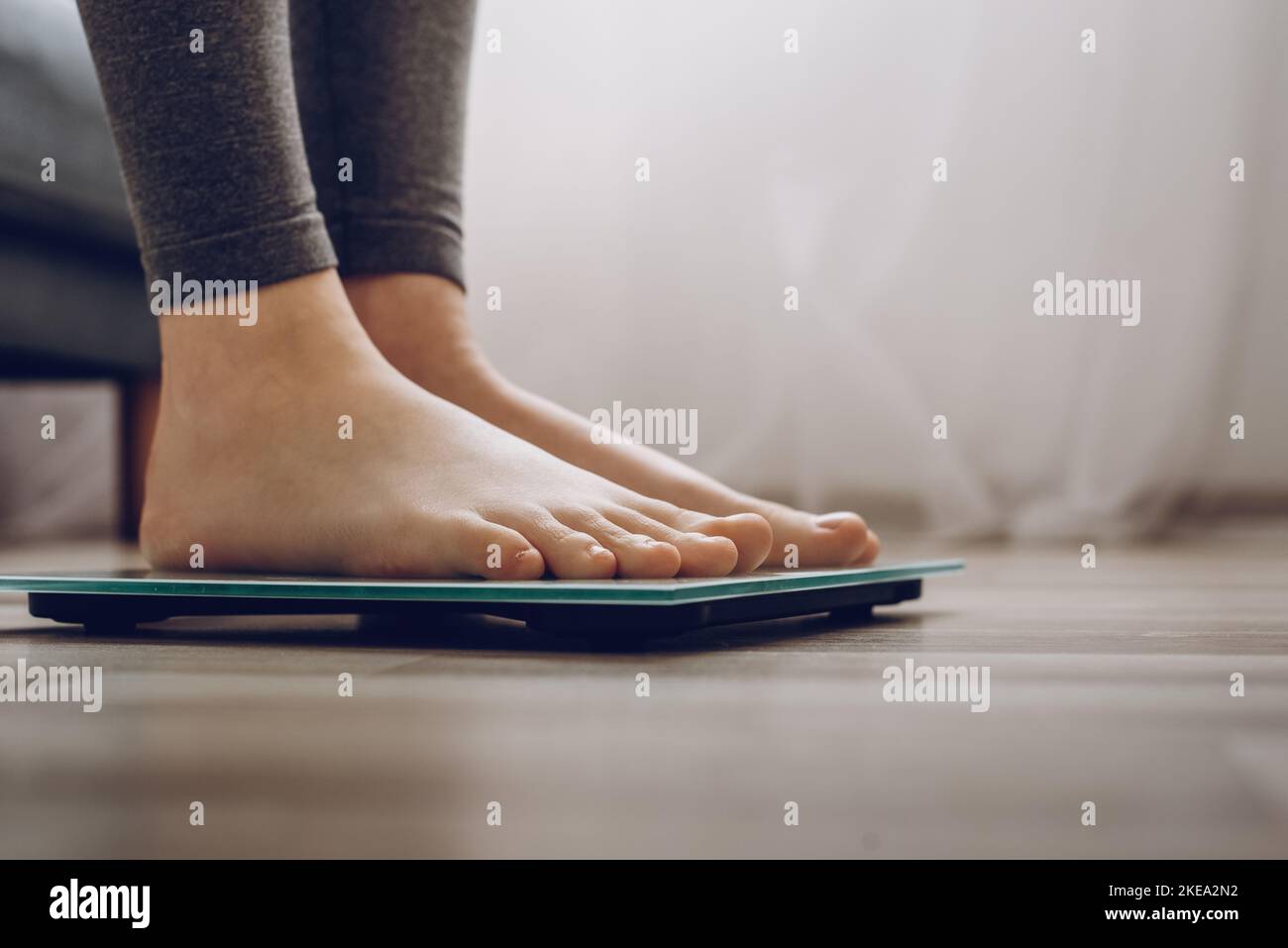 Side view of unrecognizable young woman weighing on scales at home ...
