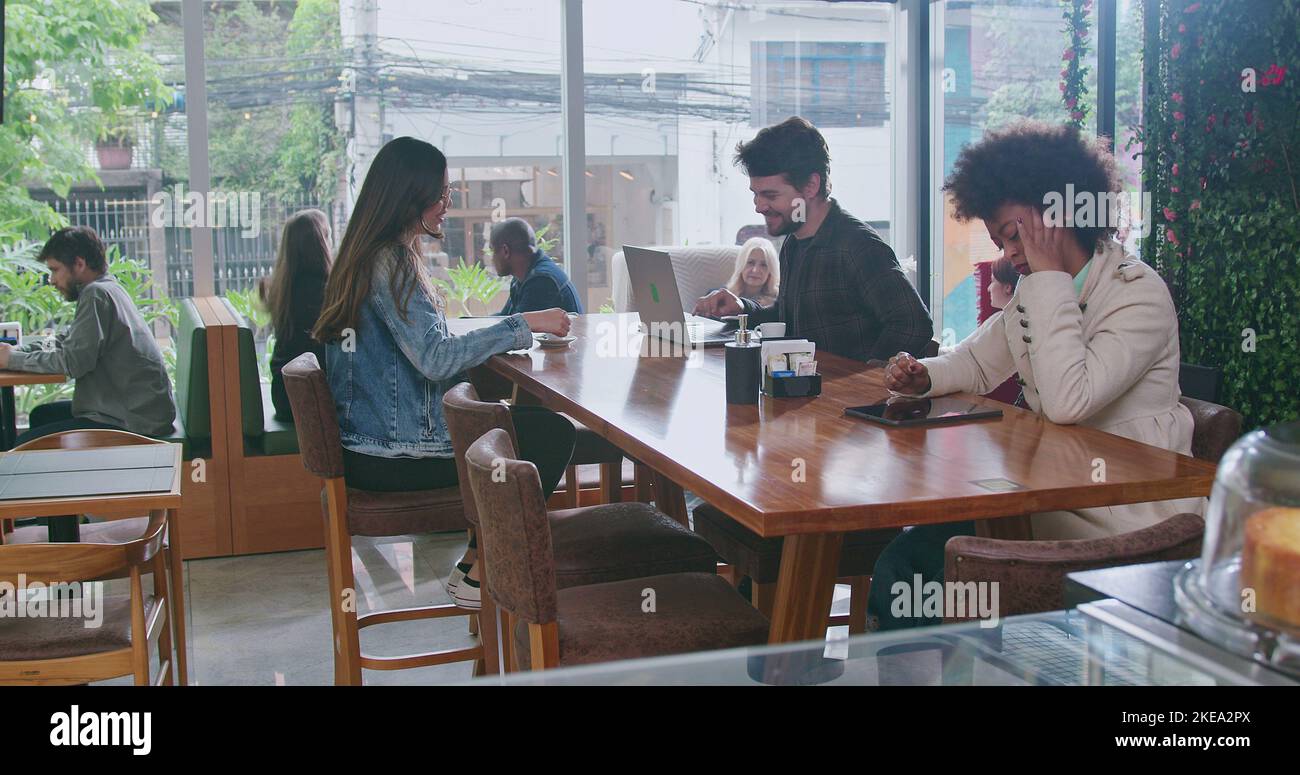 Group of people inside coffee shop. Female friend handing espresso to ...