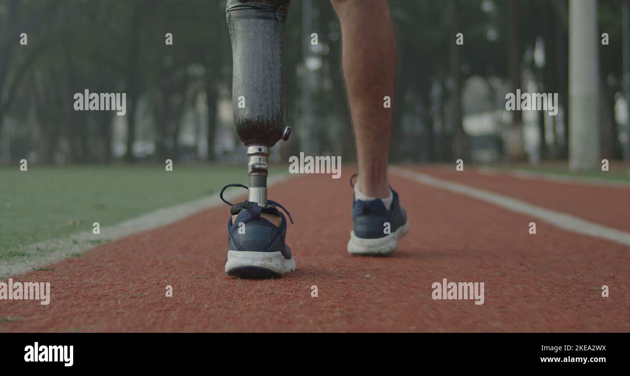 Back view of a disabled athlete man with prosthetic leg walking on ...