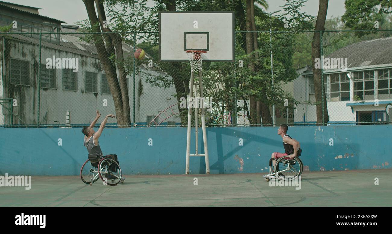 Two paraplegic disabled athletes playing basketball outdoors passing ...