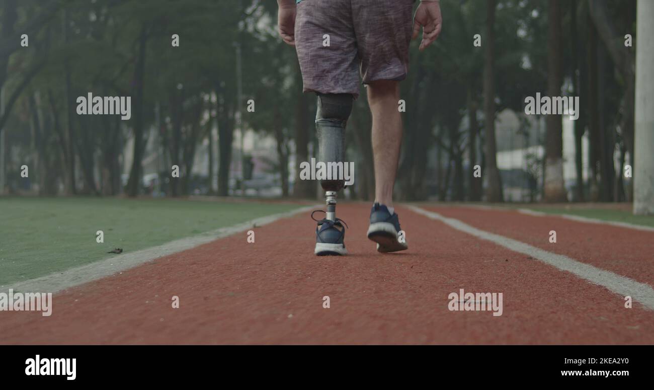 Back view of a disabled athlete man with prosthetic leg walking on ...