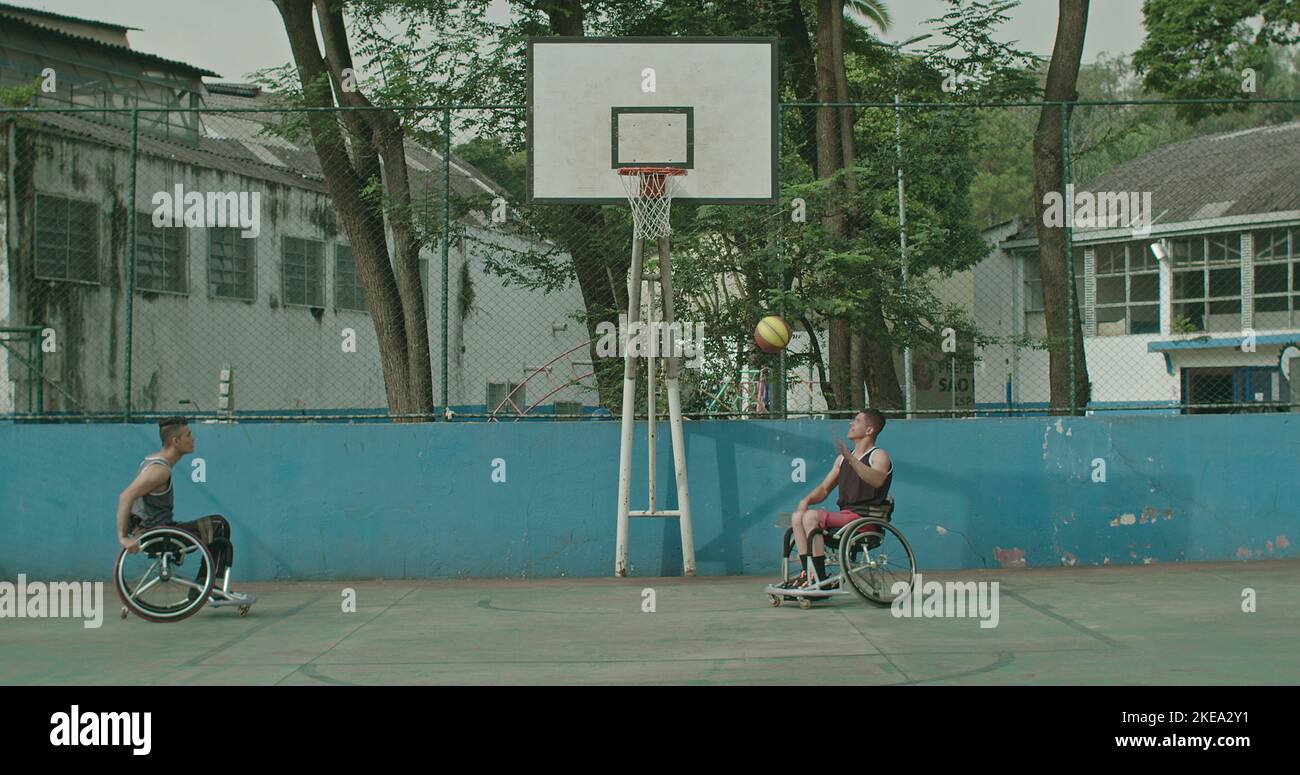 Two paraplegic disabled athletes playing basketball outdoors passing ...