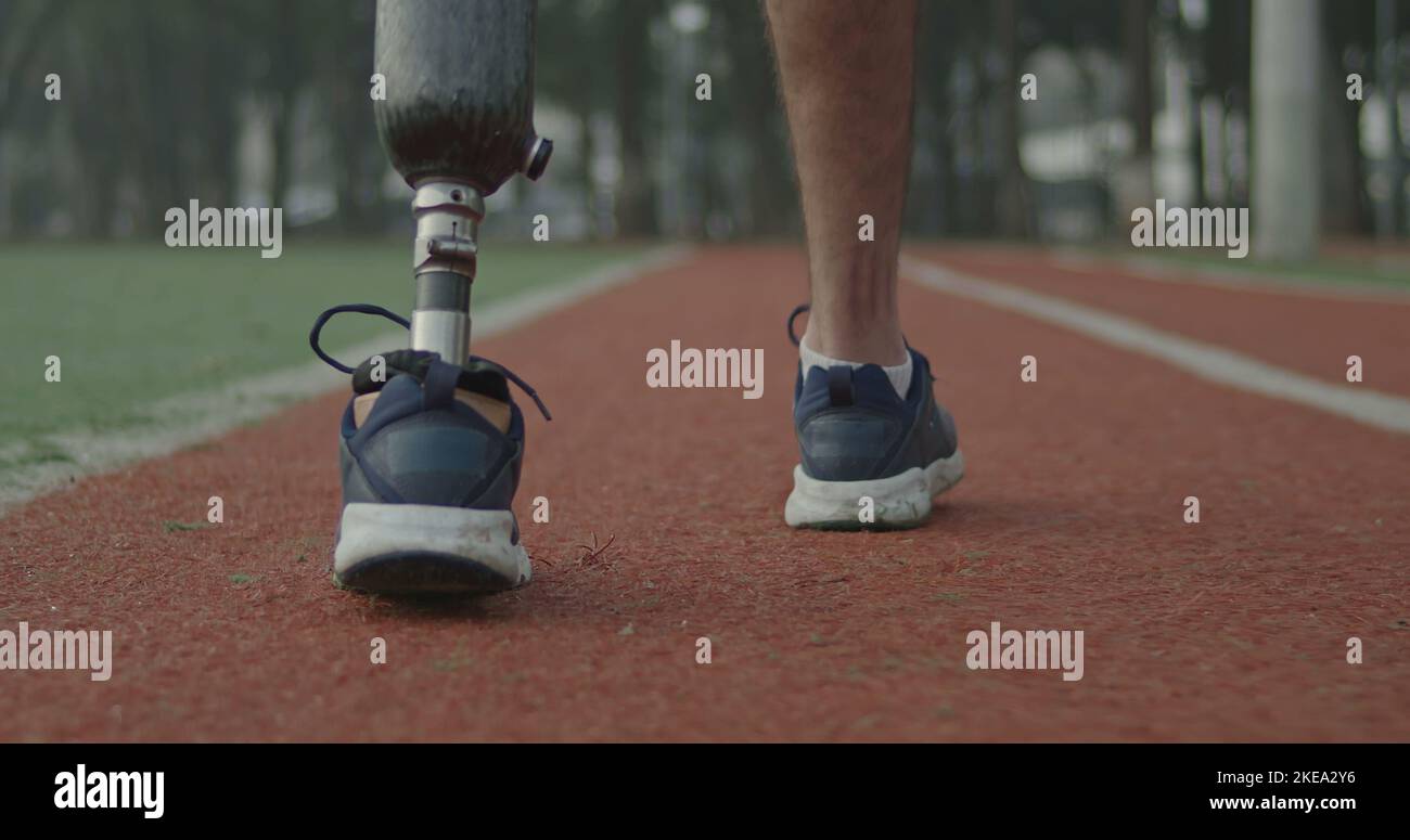 Back view of a disabled athlete man with prosthetic leg walking on ...