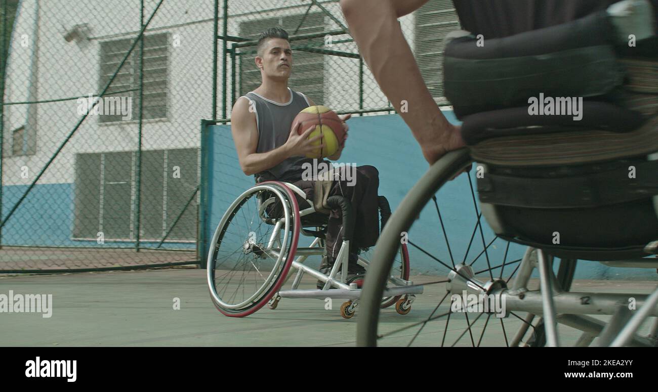 Two paraplegic disabled athletes playing basketball outdoors passing ...