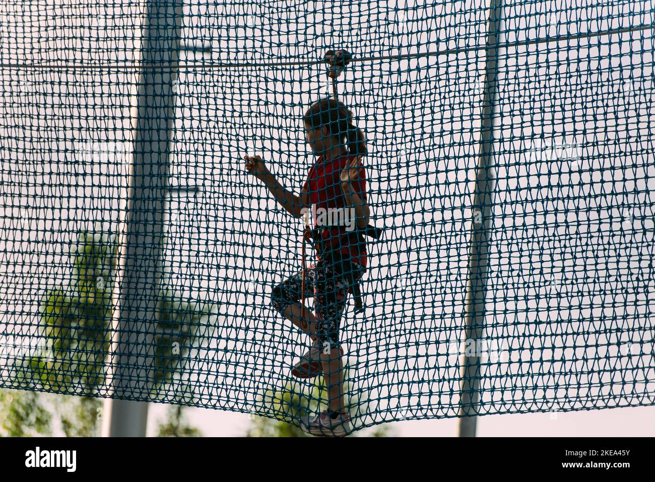 Young kid making her way through the net bridge in the adventure park ...