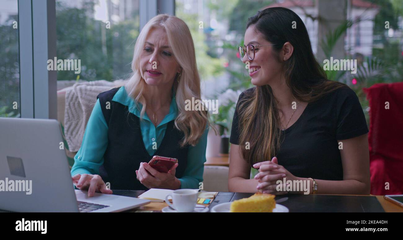 Mature woman boss explaining work to female employee at cafe business ...