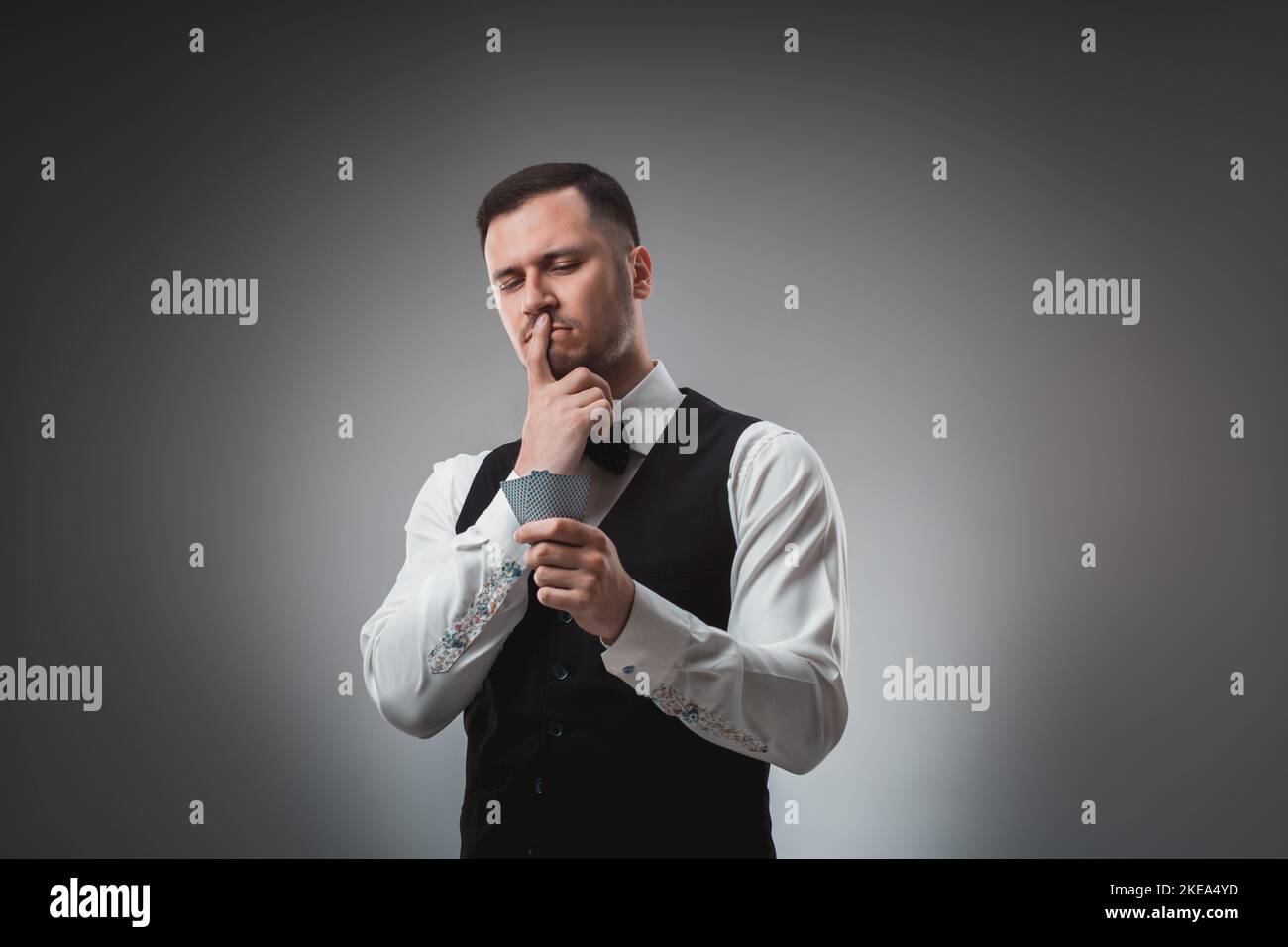 Young man in shirt and waistcoat watch his poker cards, studio shot ...