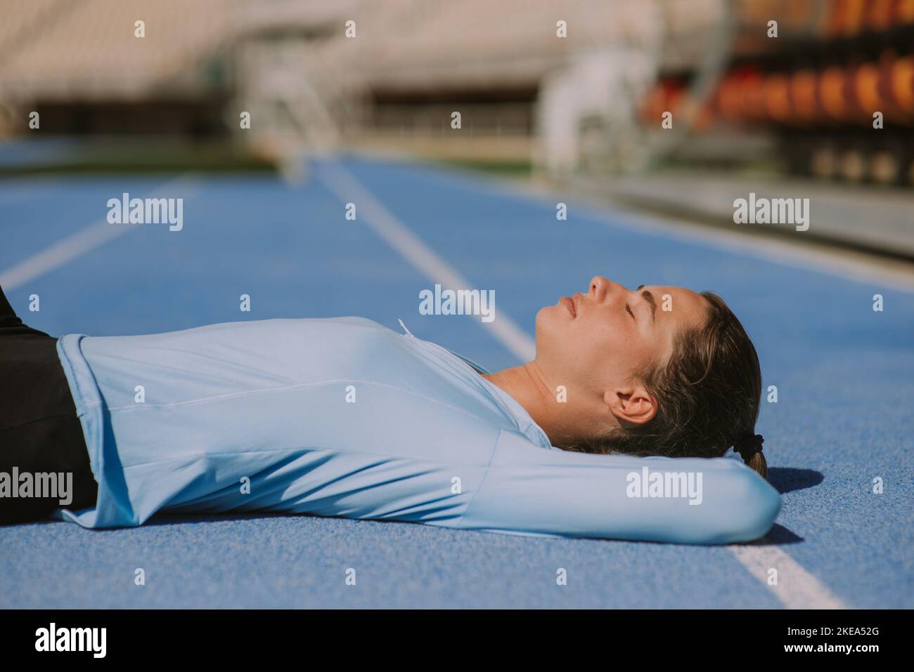 A tired attractive girl lying down on a blue sports track. She is ...