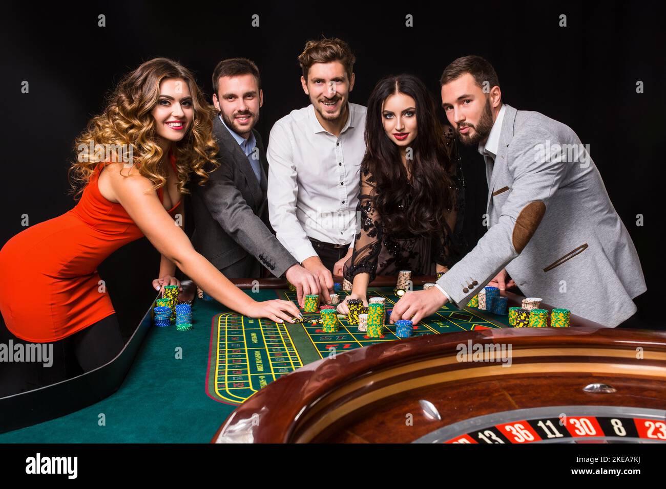 Group of young people behind roulette table on black background Stock ...