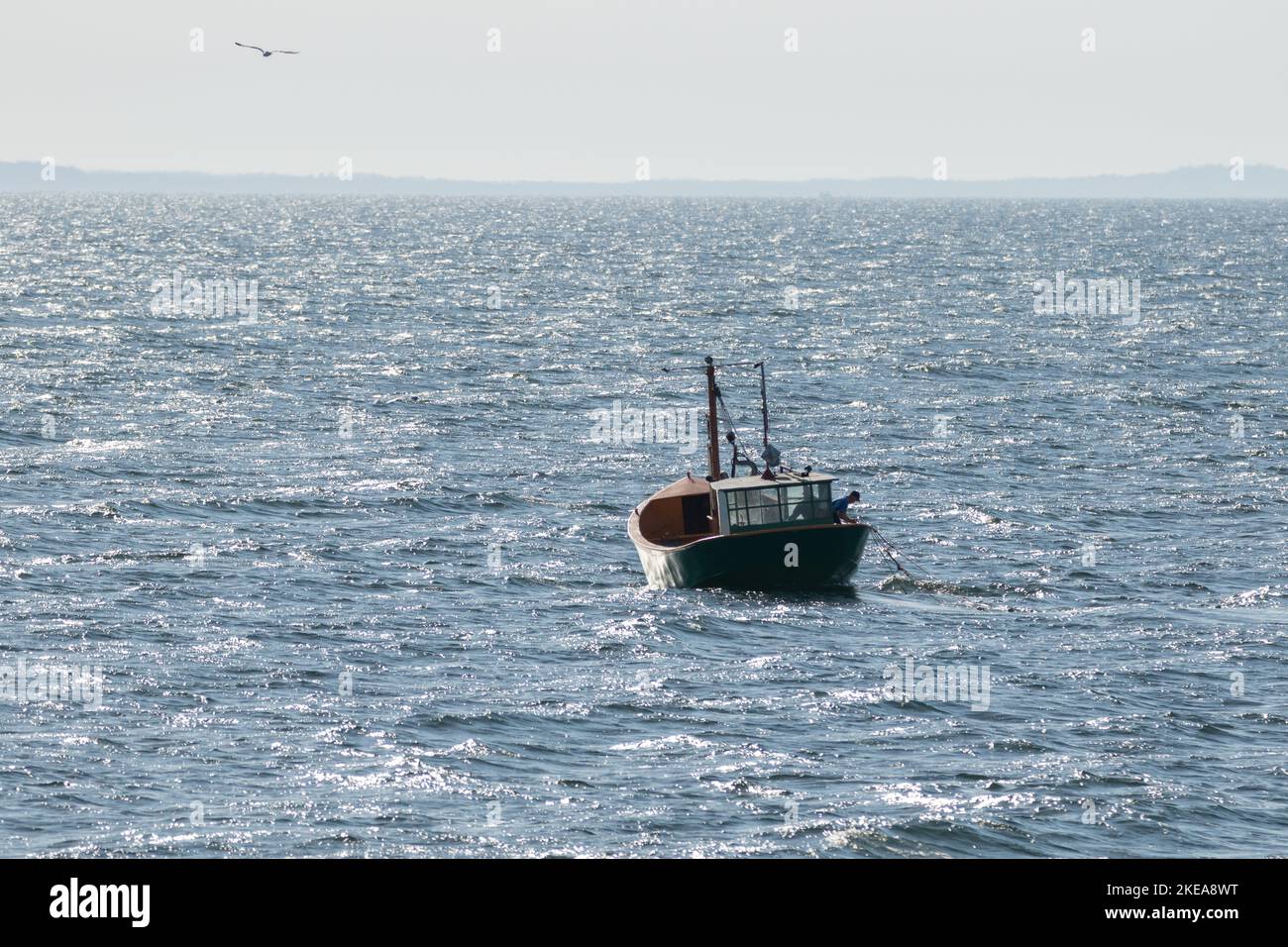 Small fishing boat on open sea with seagull flying above the waves ...
