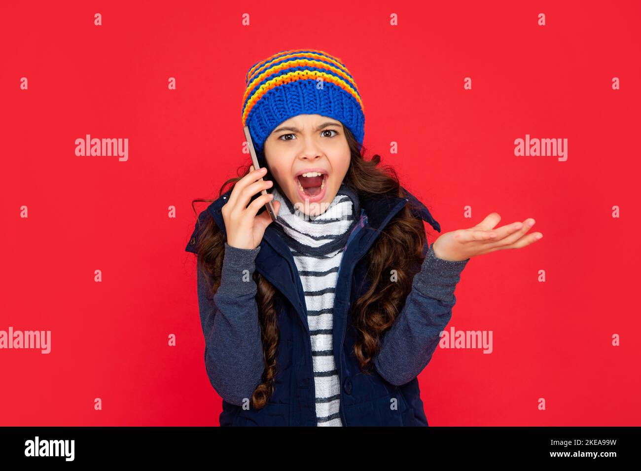 unpleased kid talking on phone in hat on red background. teen girl in ...