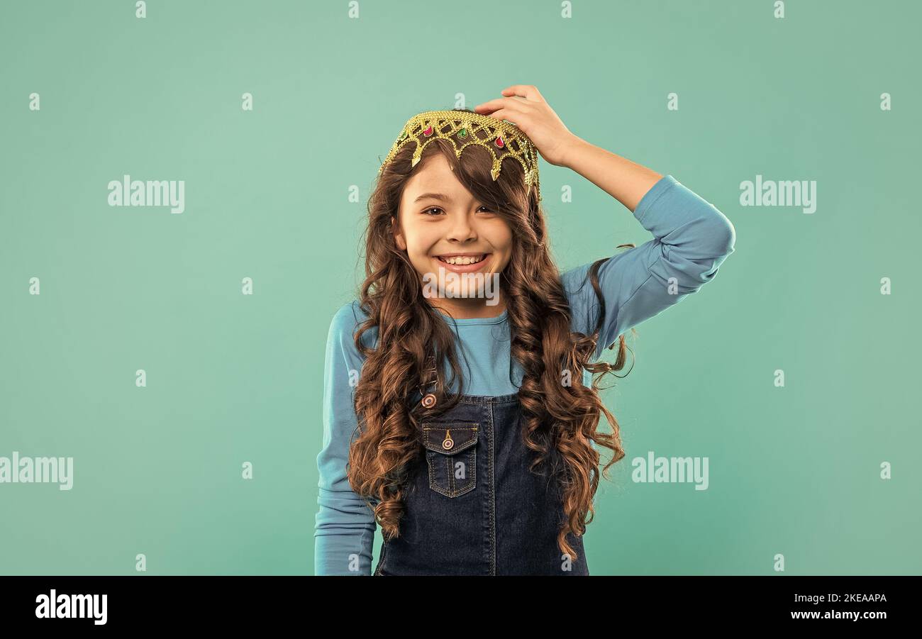 cheerful child with curly hair in queen crown on blue background ...