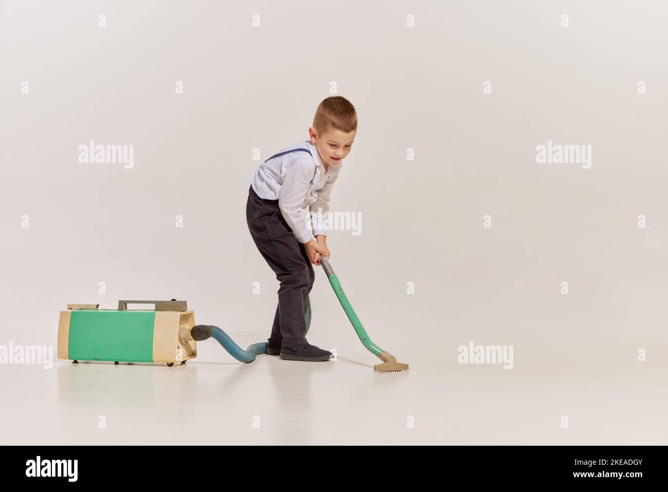 Portrait of cheerful little boy cleaning house with vacuum cleaner ...