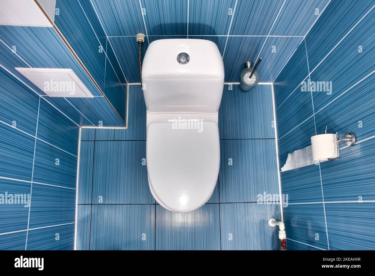 white toilet with closed lid in toilet with blue tiled wall. View of ...