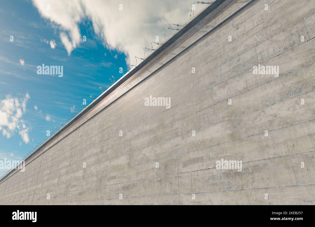 A massively high concrete security boundary wall topped with barbed ...
