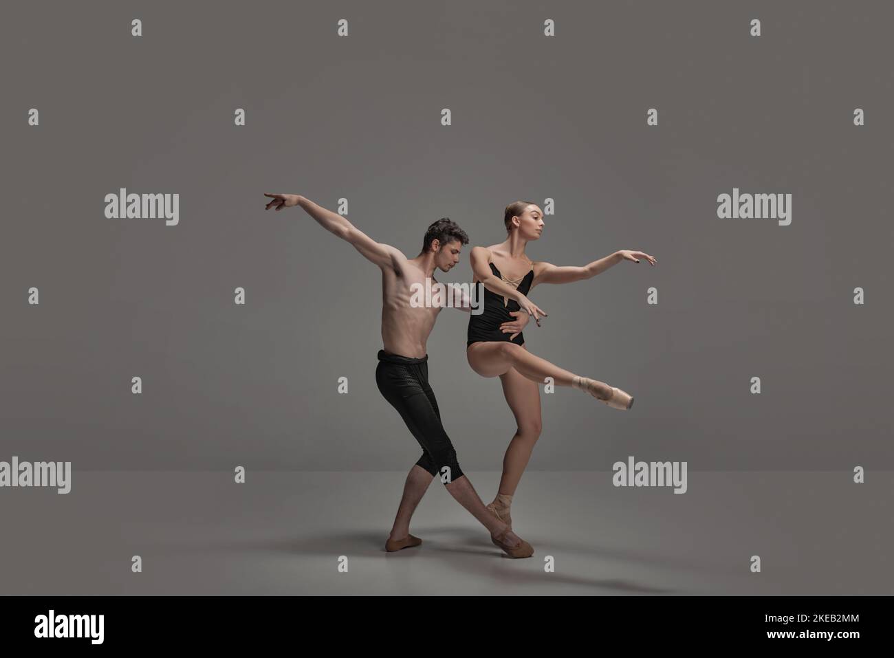 Young man and woman, ballet dancers performing isolated over dark grey ...
