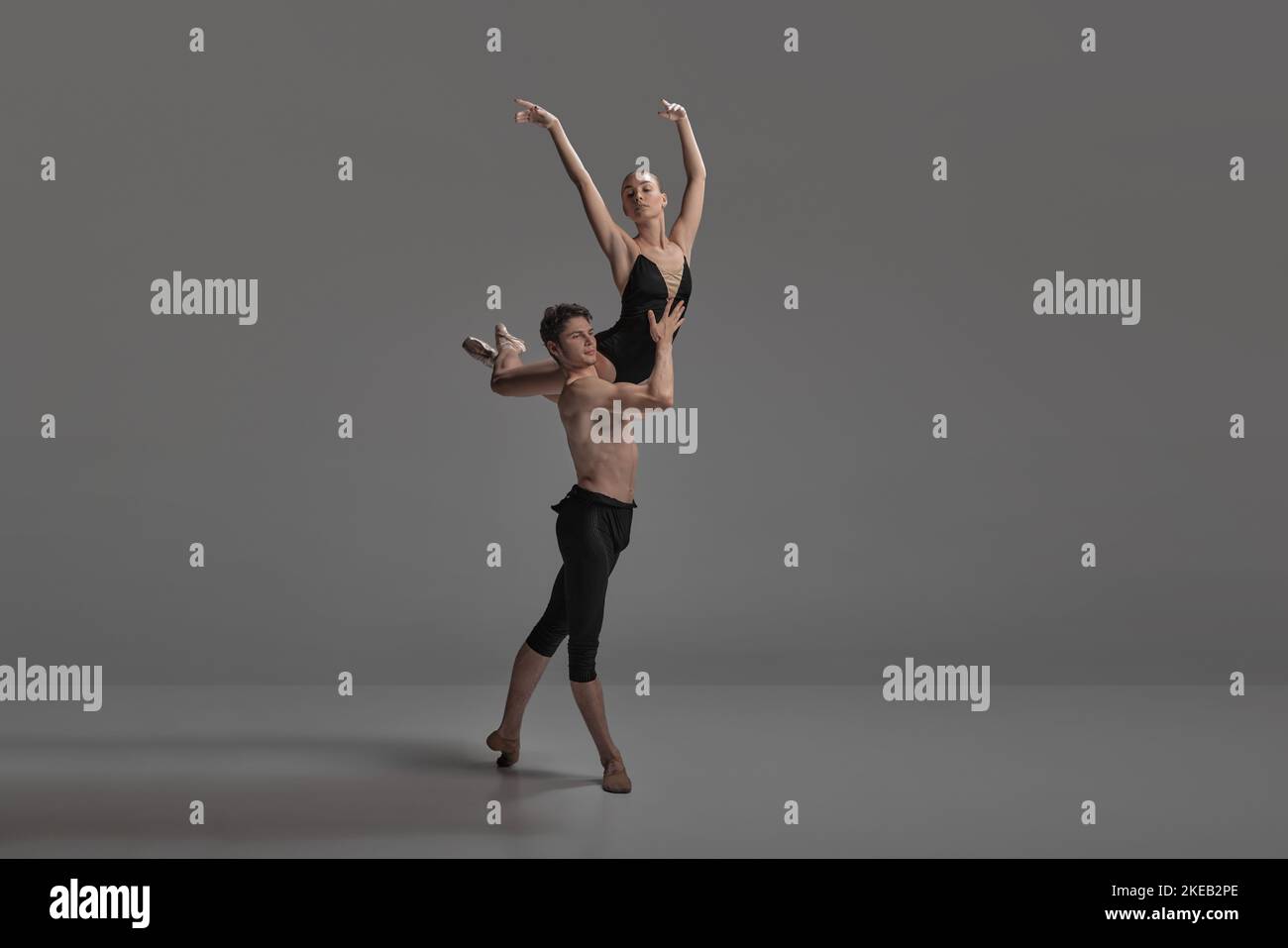 Young man and woman, ballet dancers performing isolated over dark grey ...