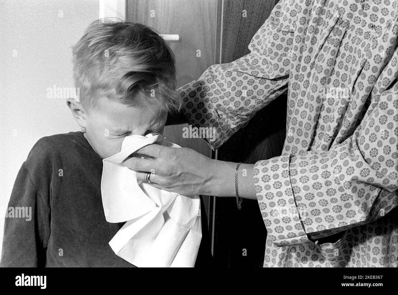 Boy in the 1950s. A mother holds a handkerchief over her sons nose as ...