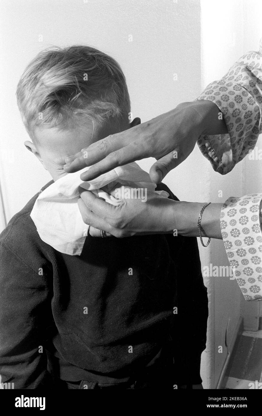 Boy in the 1950s. A mother holds a handkerchief over her sons nose as ...