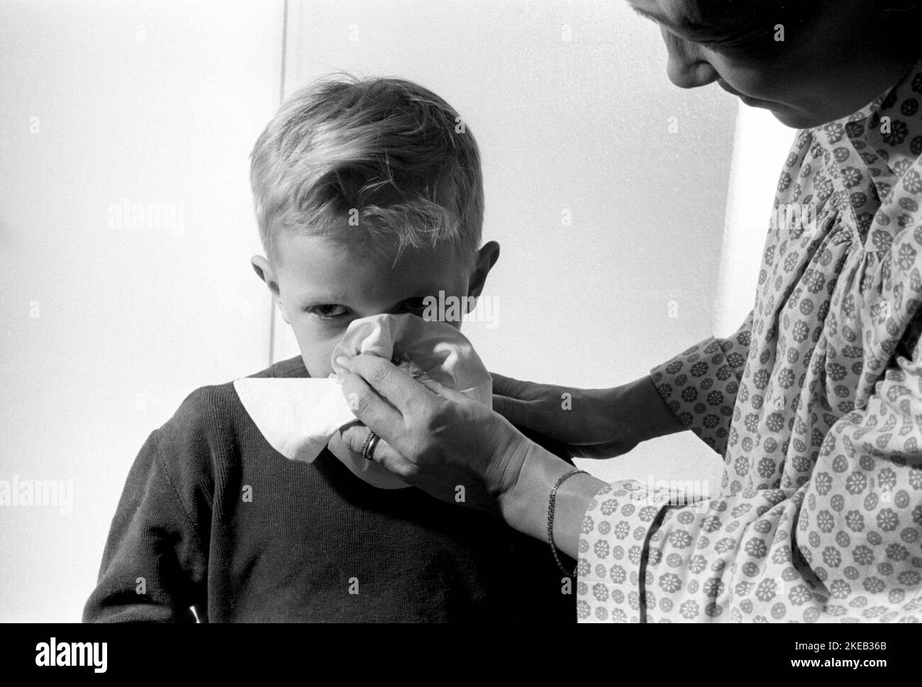 Boy in the 1950s. A mother holds a handkerchief over her sons nose as ...