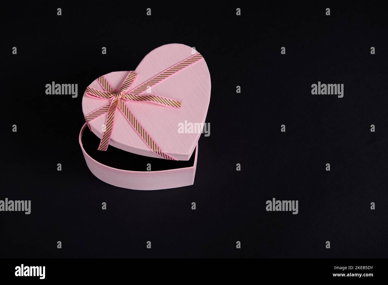 Top view of an open heart shaped pink gift box with tied bow on black ...
