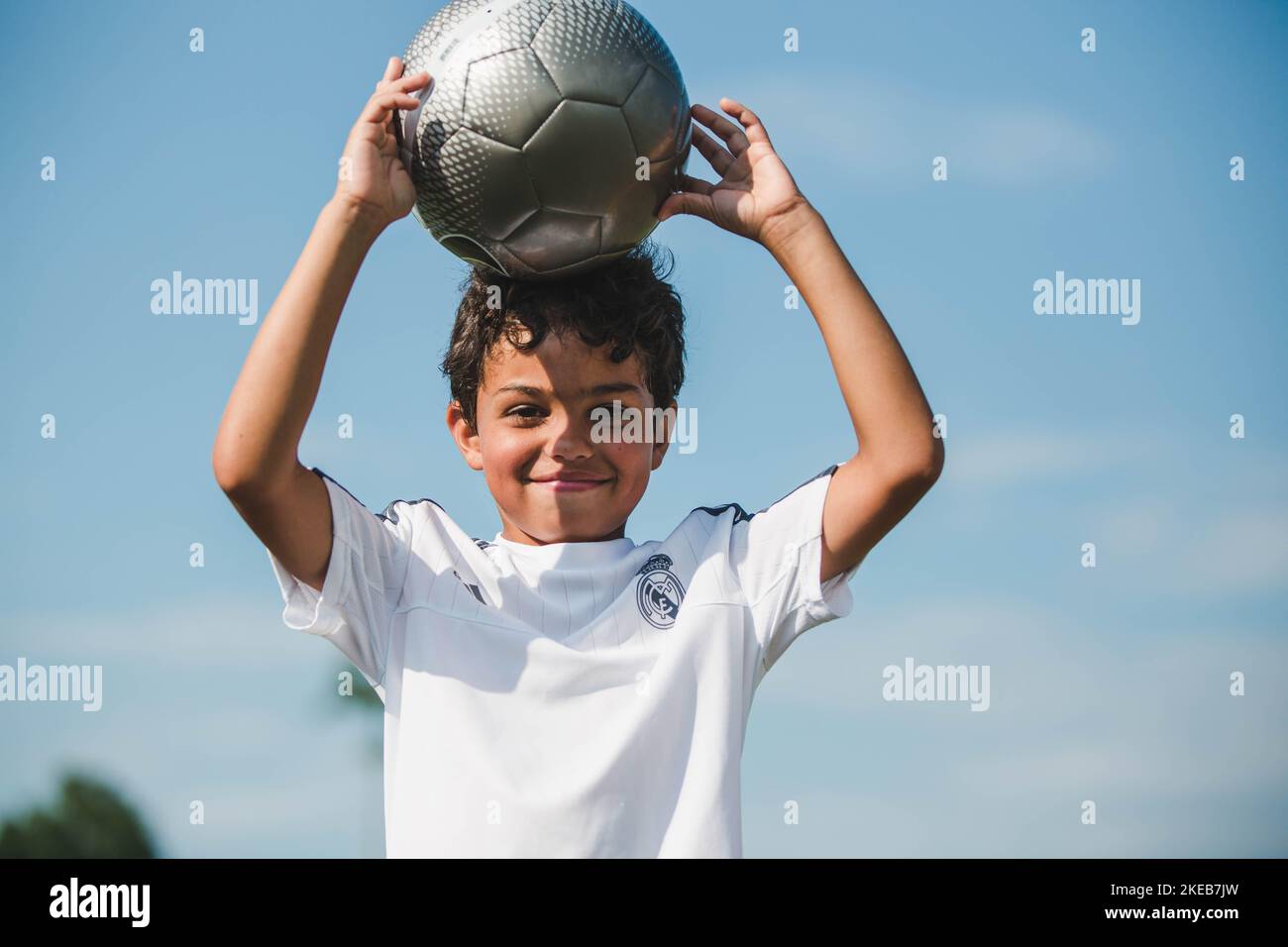 An adorable young boy holding a gray soccer ball on his head and ...